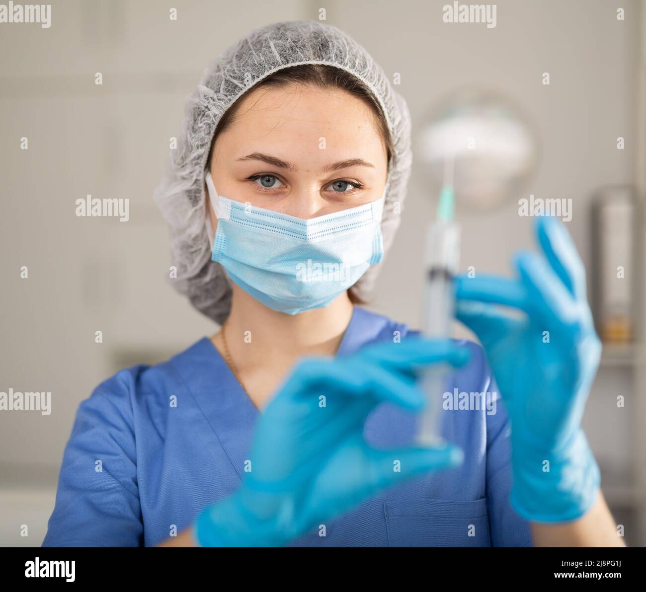 Young female nurse in a protective mask prepared a syringe with ...