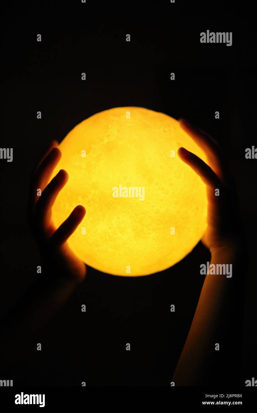 Two hands holding a yellow full moon on a dark background. Soft focus ...