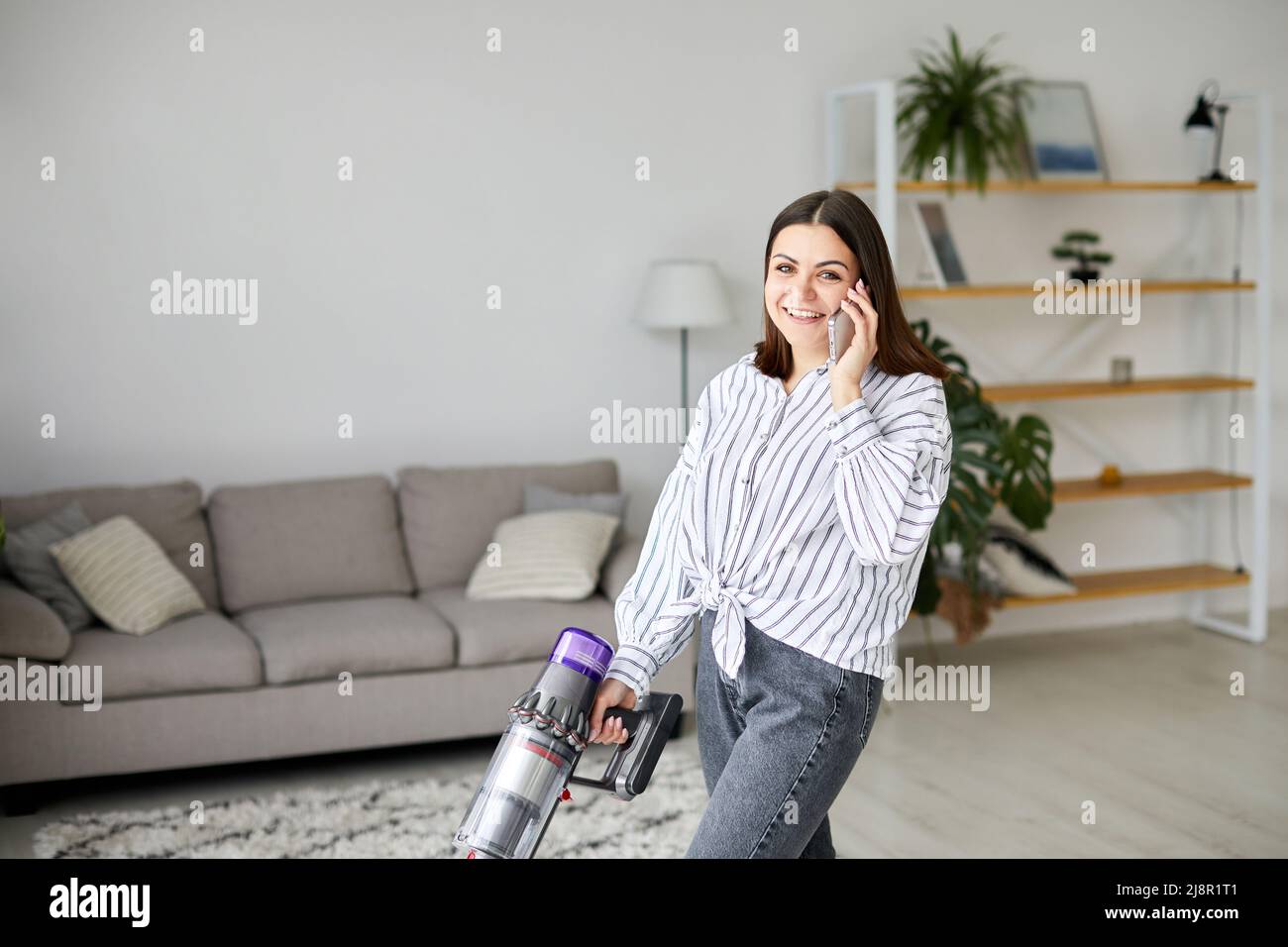 Happy cheerful young Caucasian beautiful woman vacuuming floor and ...