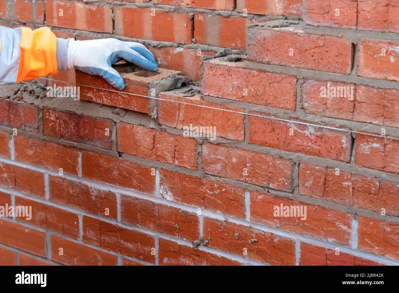 Bricklayer in safety vest and a helmet laying a brick wall using a ...