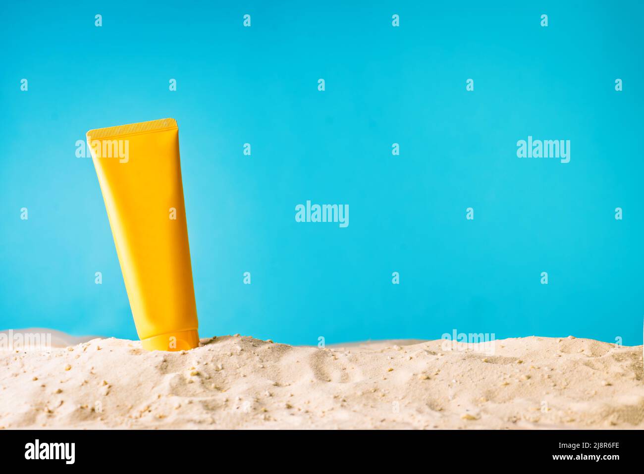 Sunscreen lotion on sandy beach, blue background, copy space. Summer ...