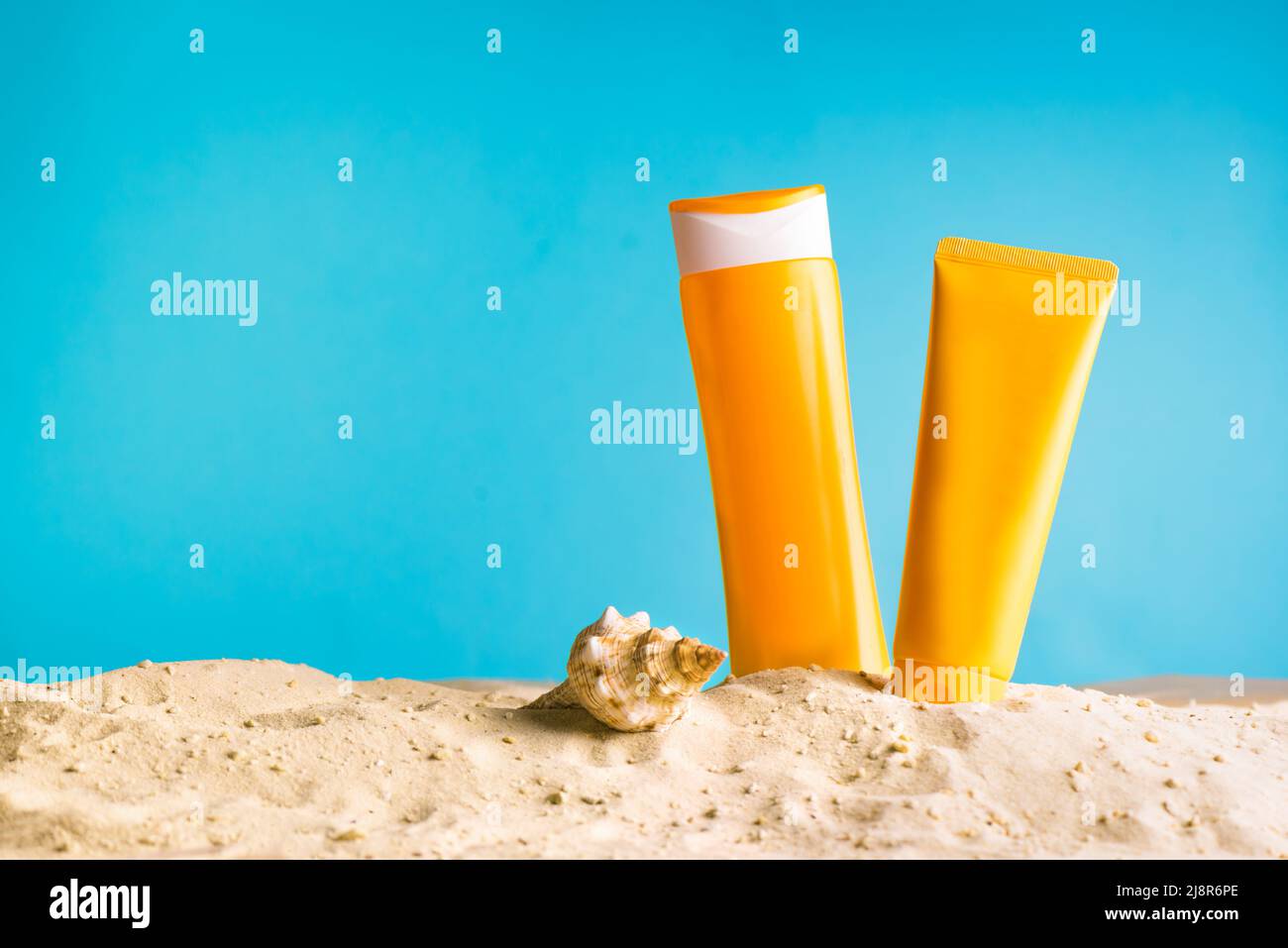 Sunscreen lotion on sandy beach, blue background, copy space. Summer ...