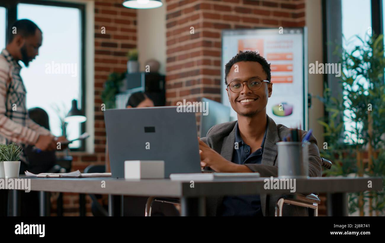 Portrait of happy man using laptop to work on company statistics, analyzing business graphs with ...