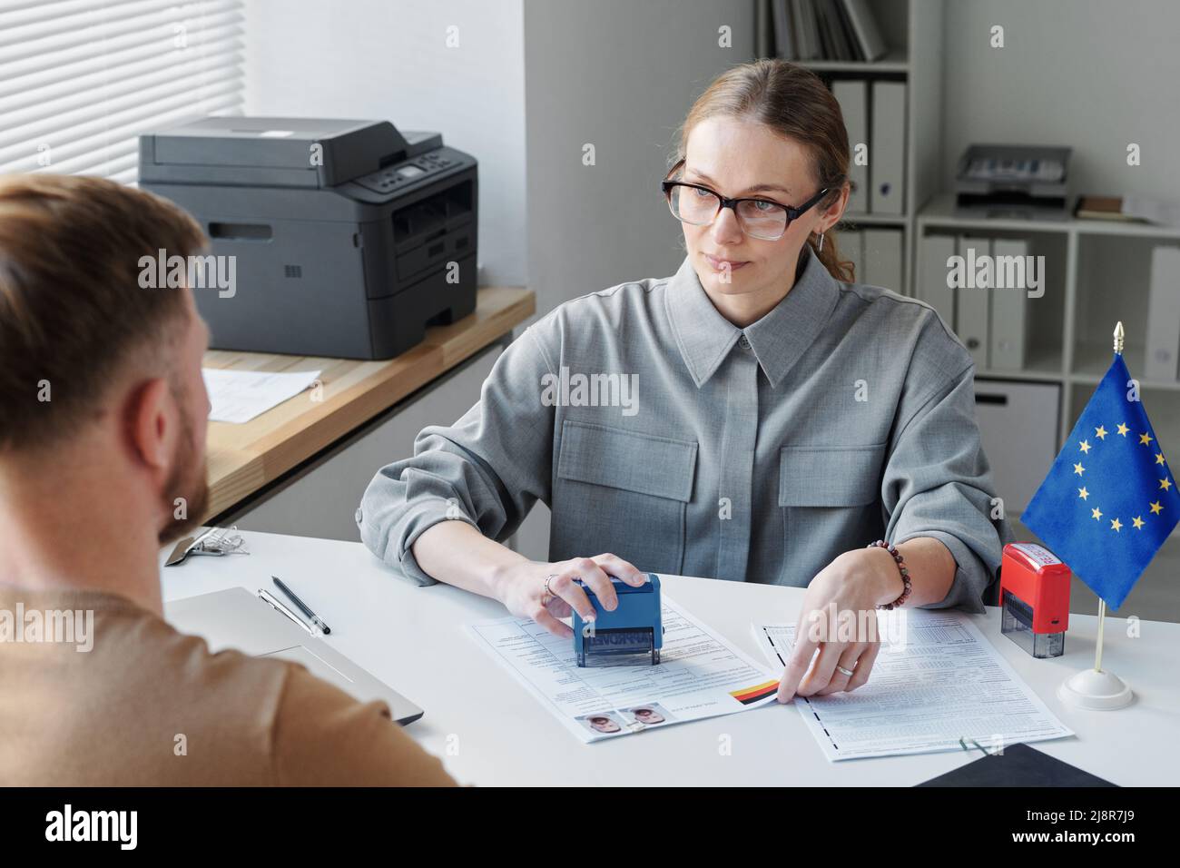 Modern consular officer sitting at table finishing interview with ...