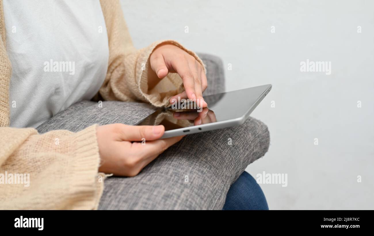 Rear view, A female relaxing at home, sitting in living room and using ...