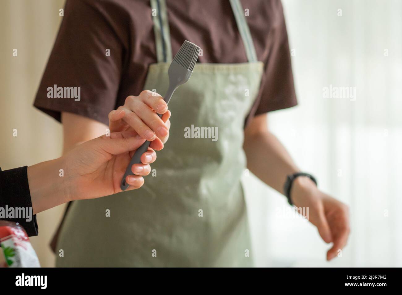 One cook passes a kitchen brush to another cook in a green apron Stock ...