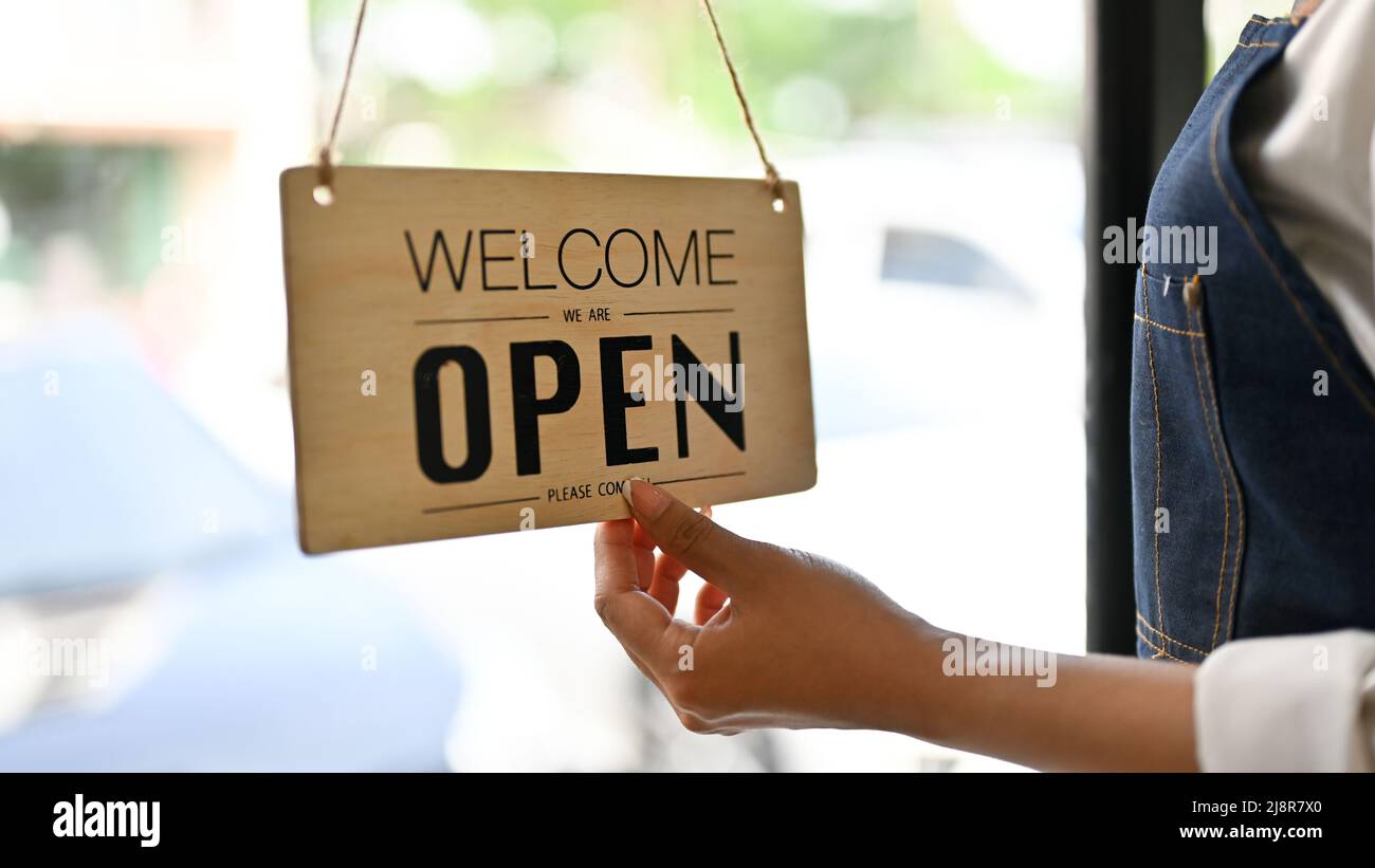Female waitress or barista hanging a welcome sign in front of the ...
