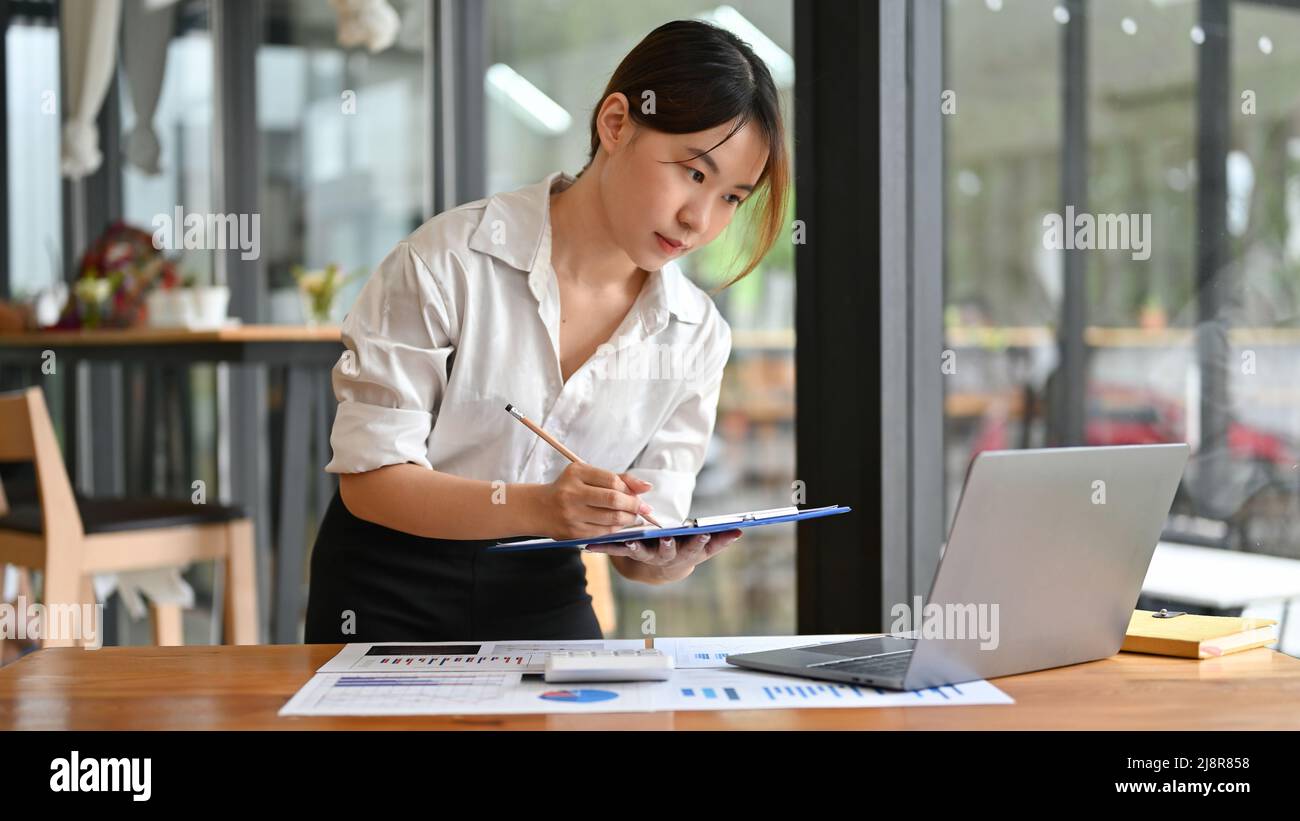 Focused Asian young female financial assistant looking the details on ...