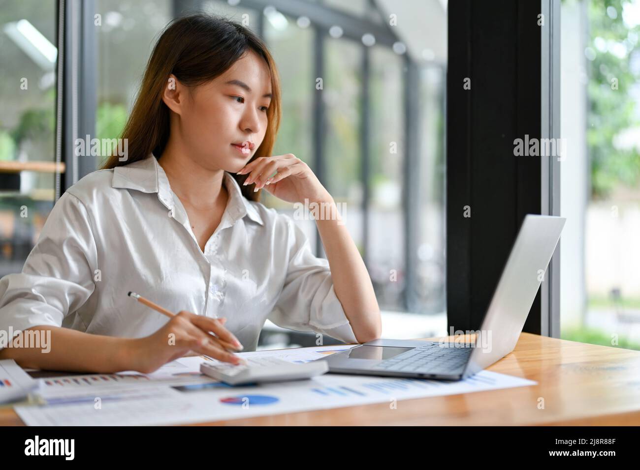 Concentrated Asian young businesswoman or female accountant focusing on ...