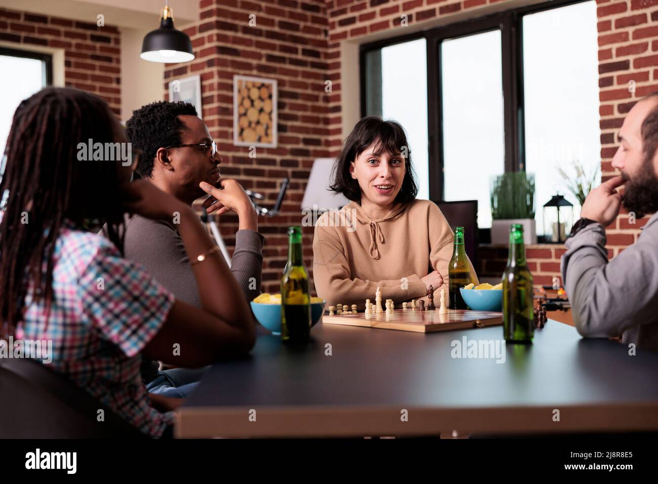 Smiling woman sitting at table in living room with multiethnic people ...