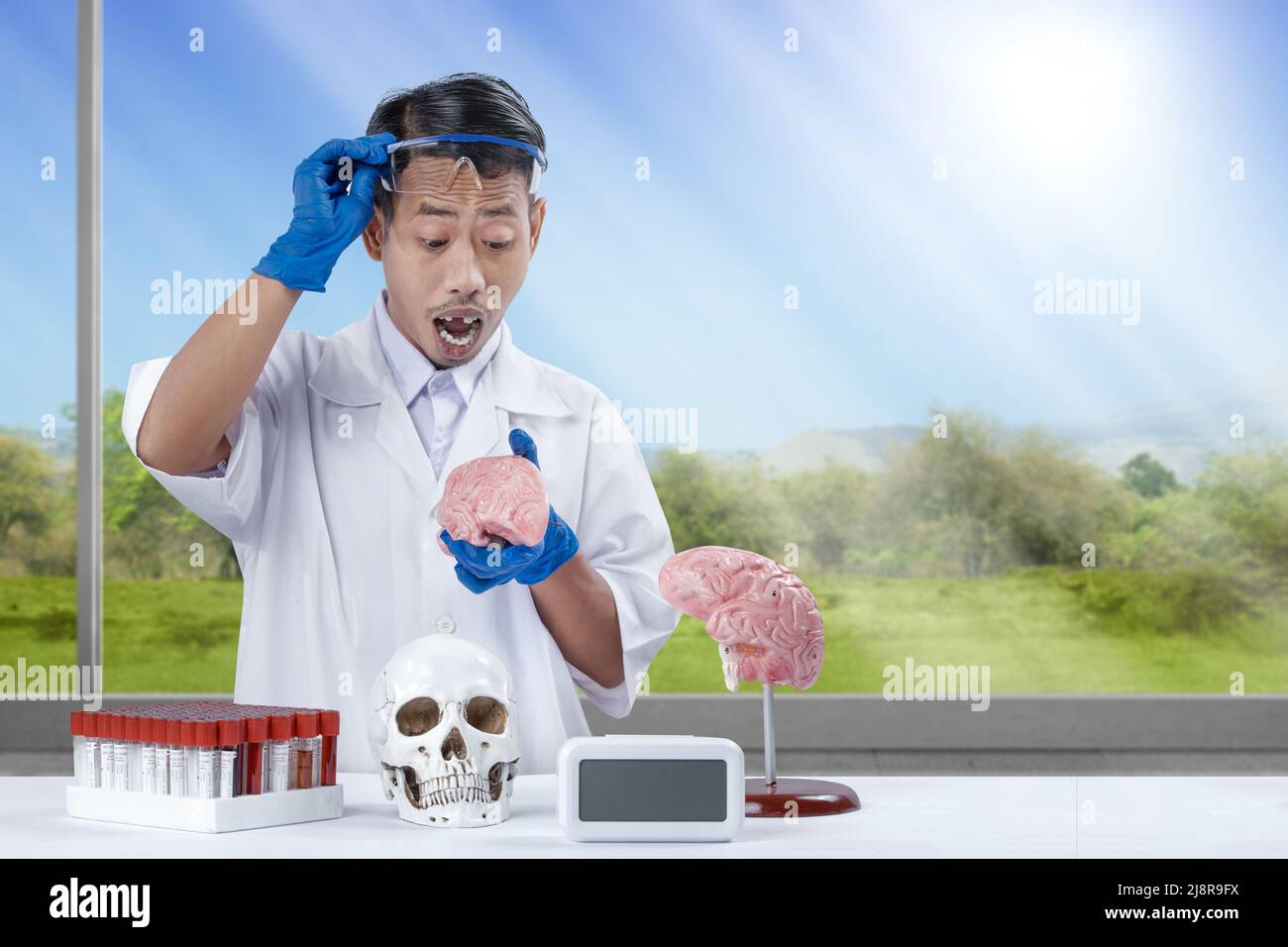 Asian nerd scientist standing and holding a human brain with a skull ...