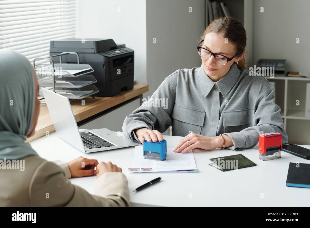 Female consular officer sitting at desk in front of Muslim visa ...
