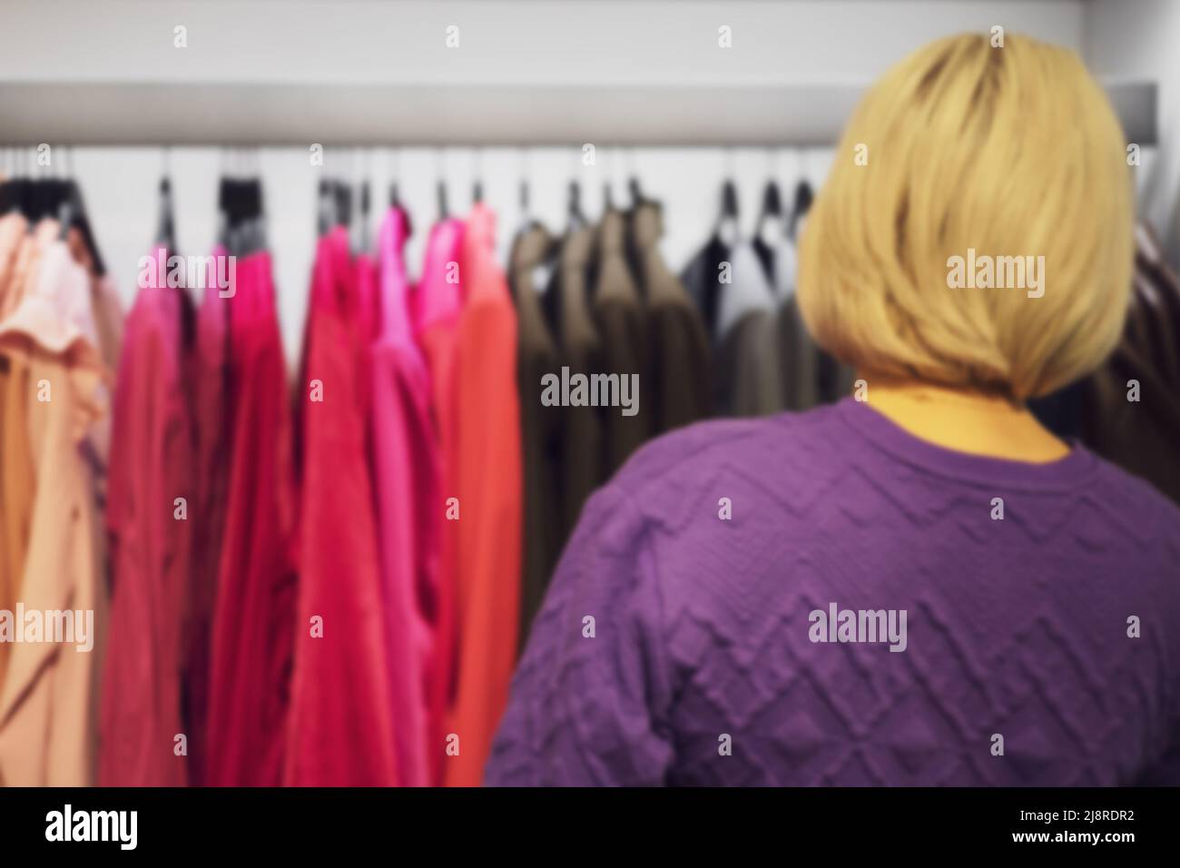 The blonde chooses jacket hanging on a hanger. Shopping in a fashion ...