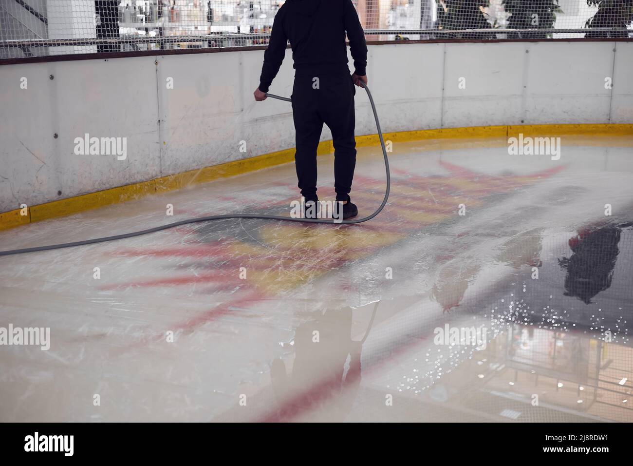 Service man pours water from hose onto an ice rink. Ice preparation ...