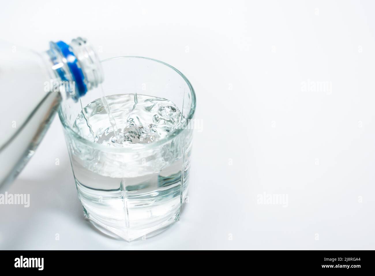 Pouring pure fresh mineral non-carbonated water into a glass beaker on a white background from a ...