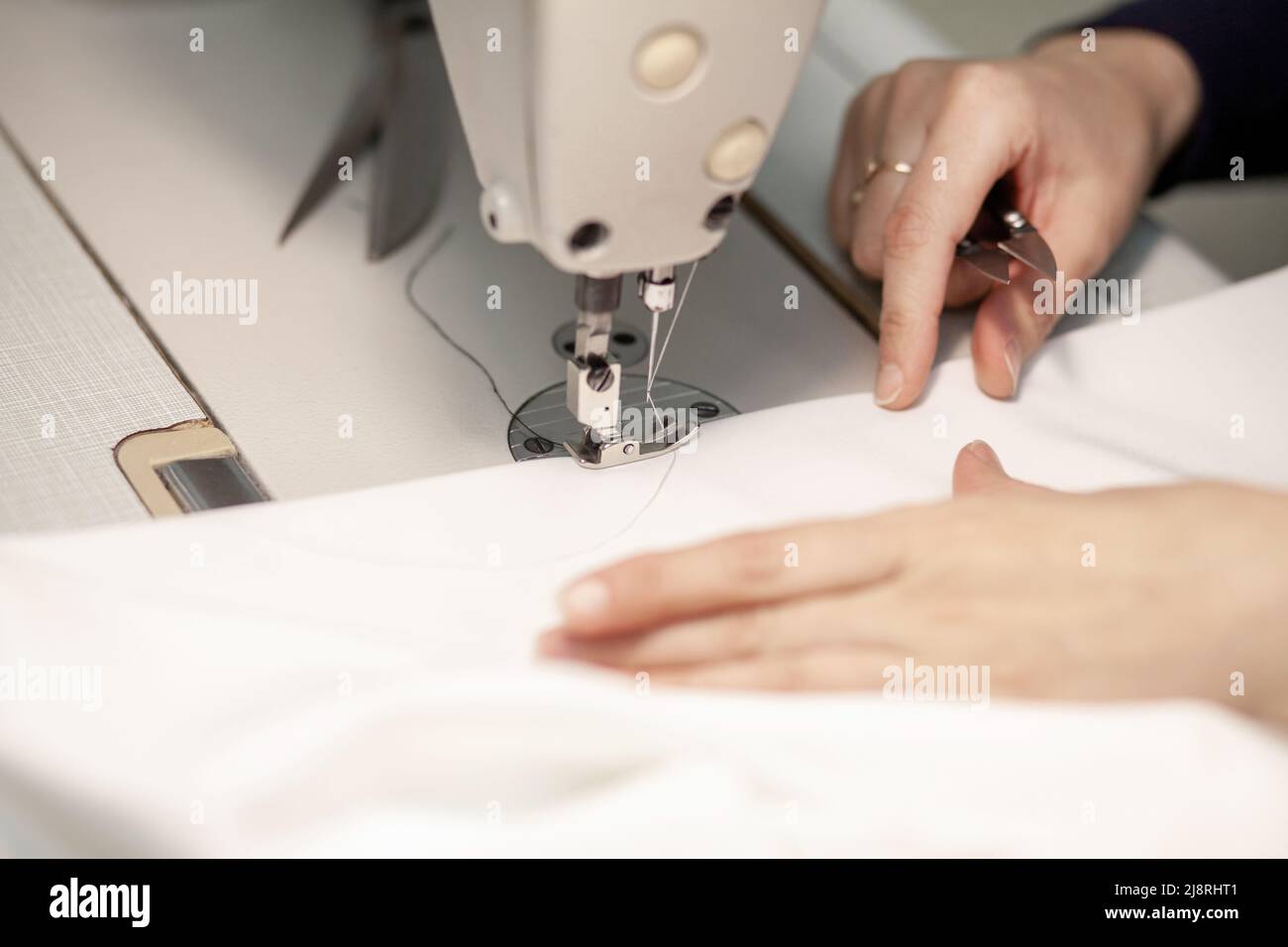 Hands of a dressmaker sewing clothes from white fabric on a sewing ...