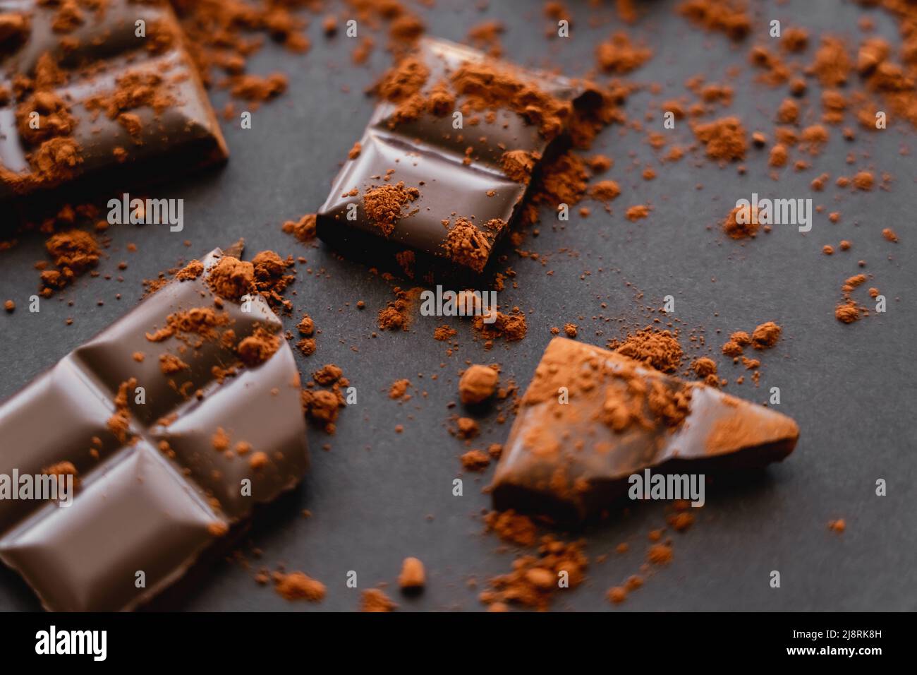 Close up view of dry cocoa powder on chocolate pieces on black ...