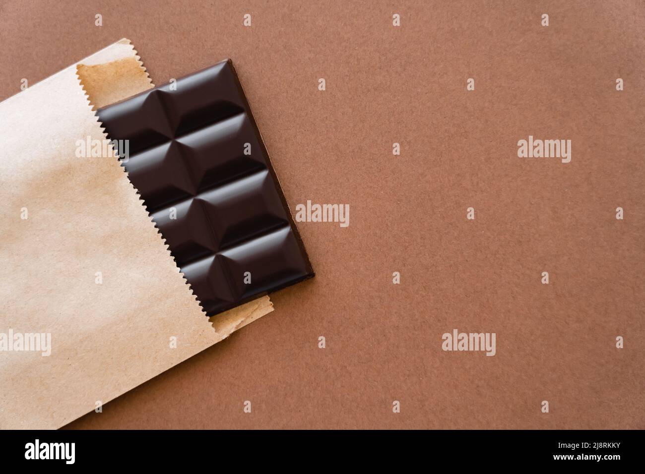 Top view of dark chocolate bar in craft package on brown background ...