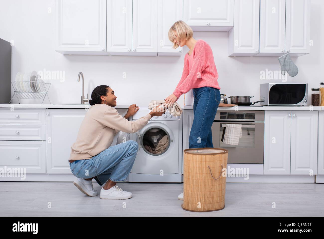 side view of smiling blonde woman passing dirty clothes to cheerful ...
