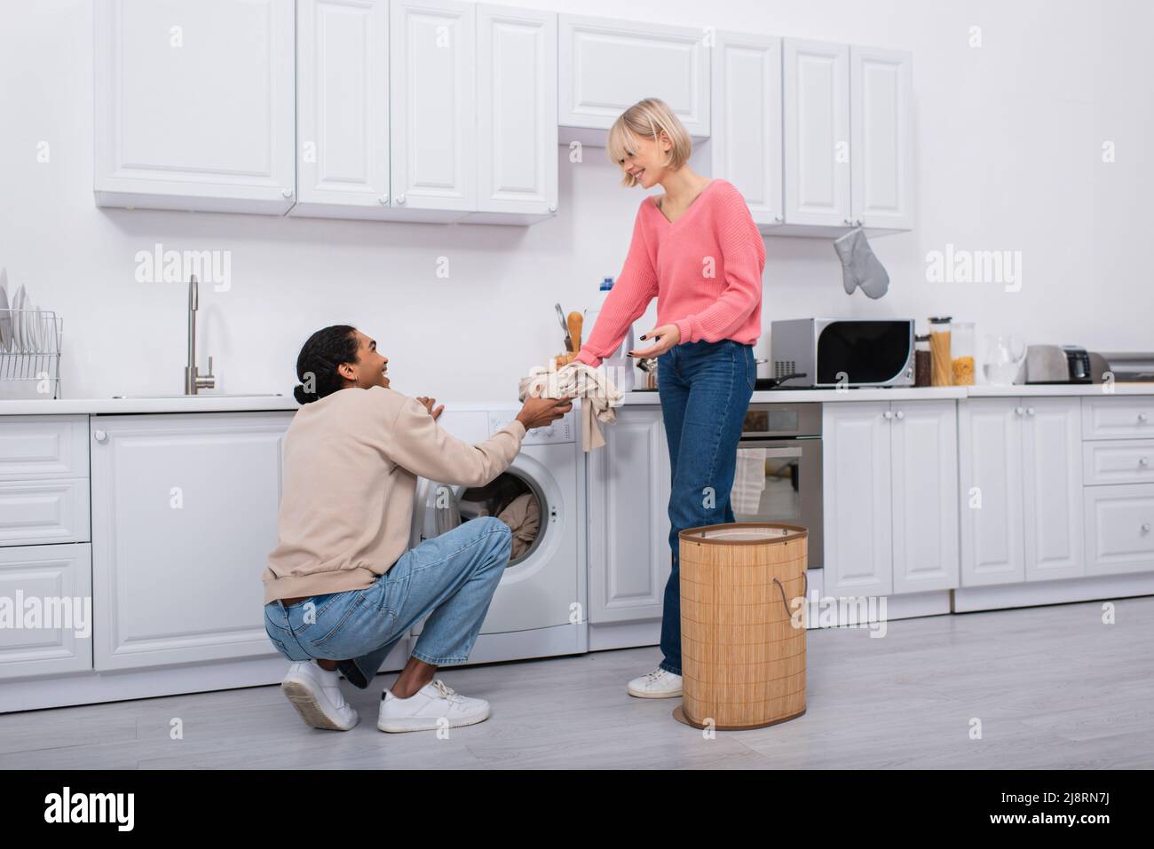 happy blonde woman passing dirty clothes to cheerful african american ...