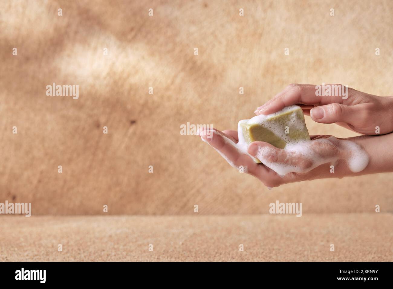 Sensitive hands of female holding soap with foam on brown background ...