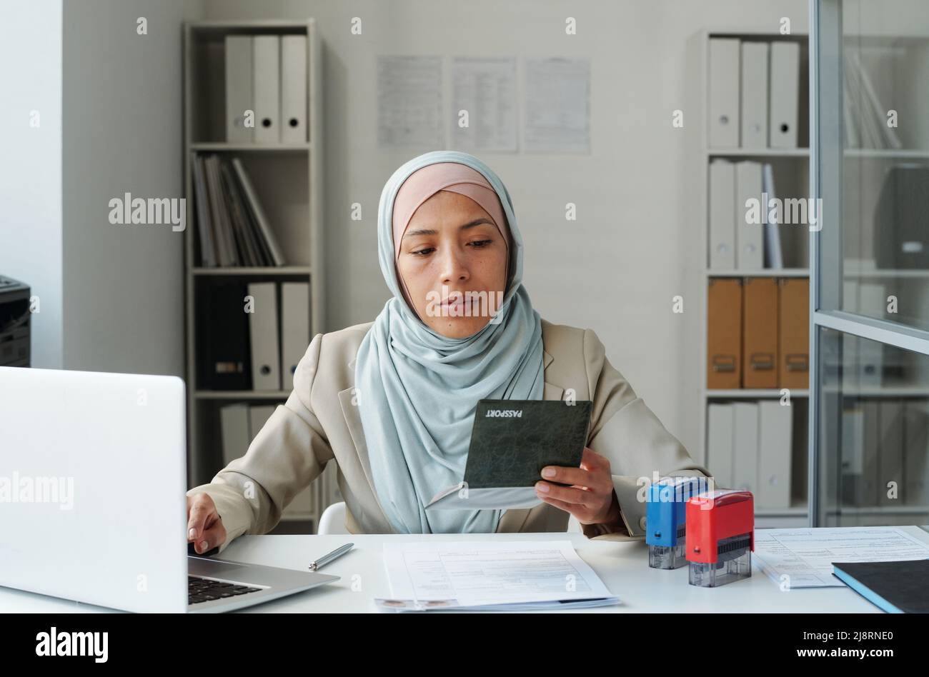 Modern Muslim woman working in embassy office adding passport ...