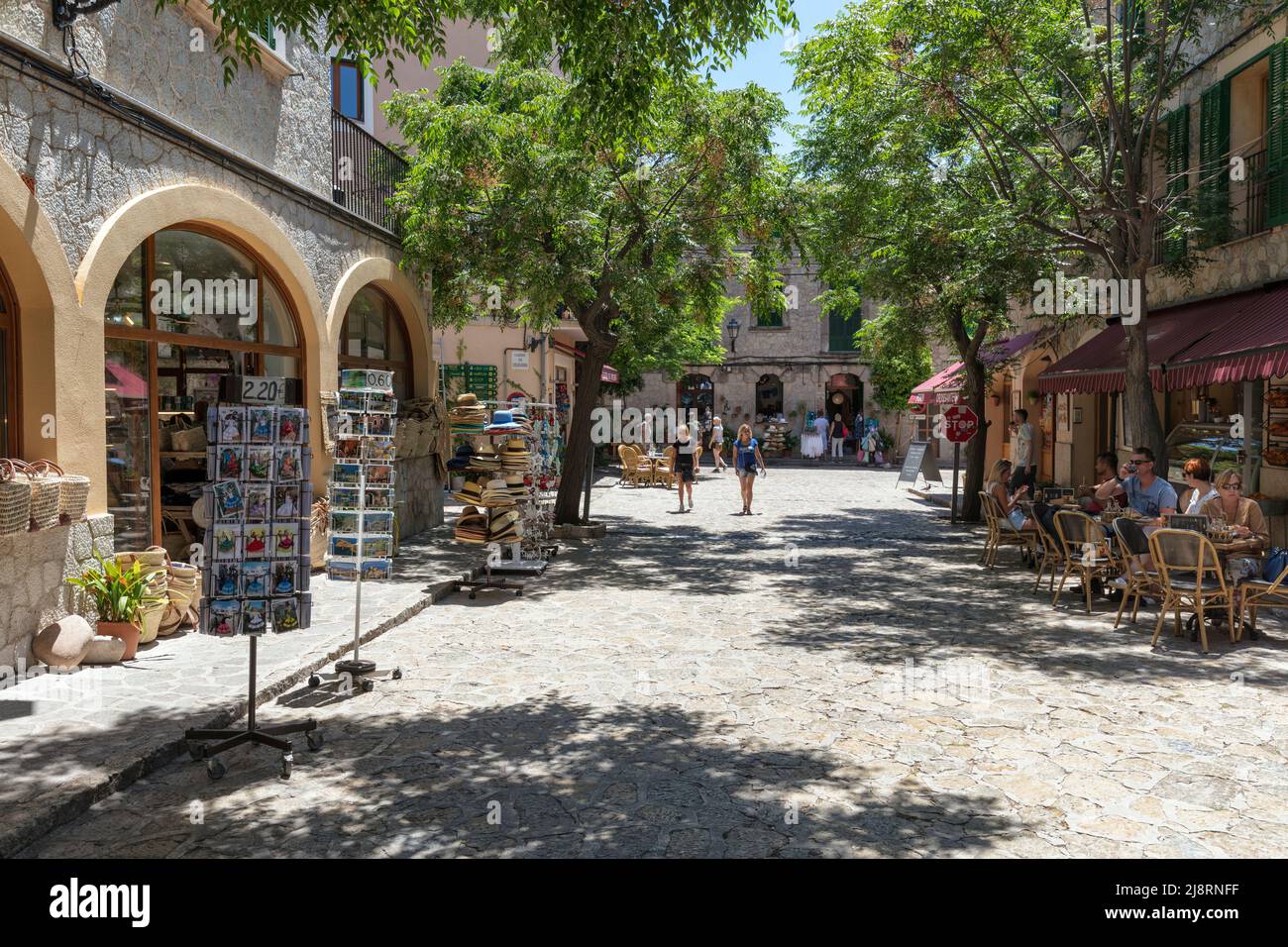 Sunlit Carrer Marques de Vivot, tree lined cobbled street, shopping ...