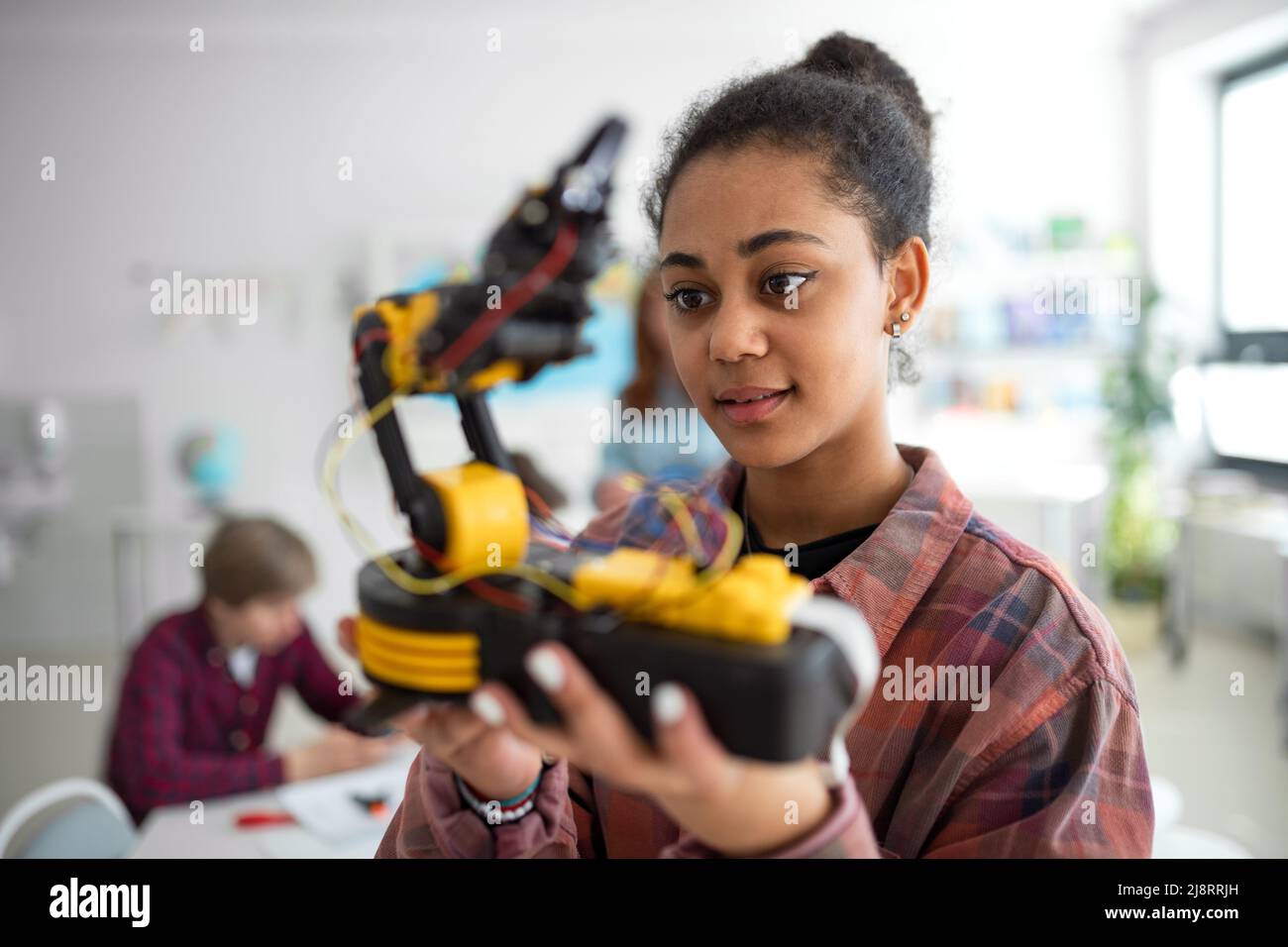 College student holding her robotic toy at robotics classroom at school ...