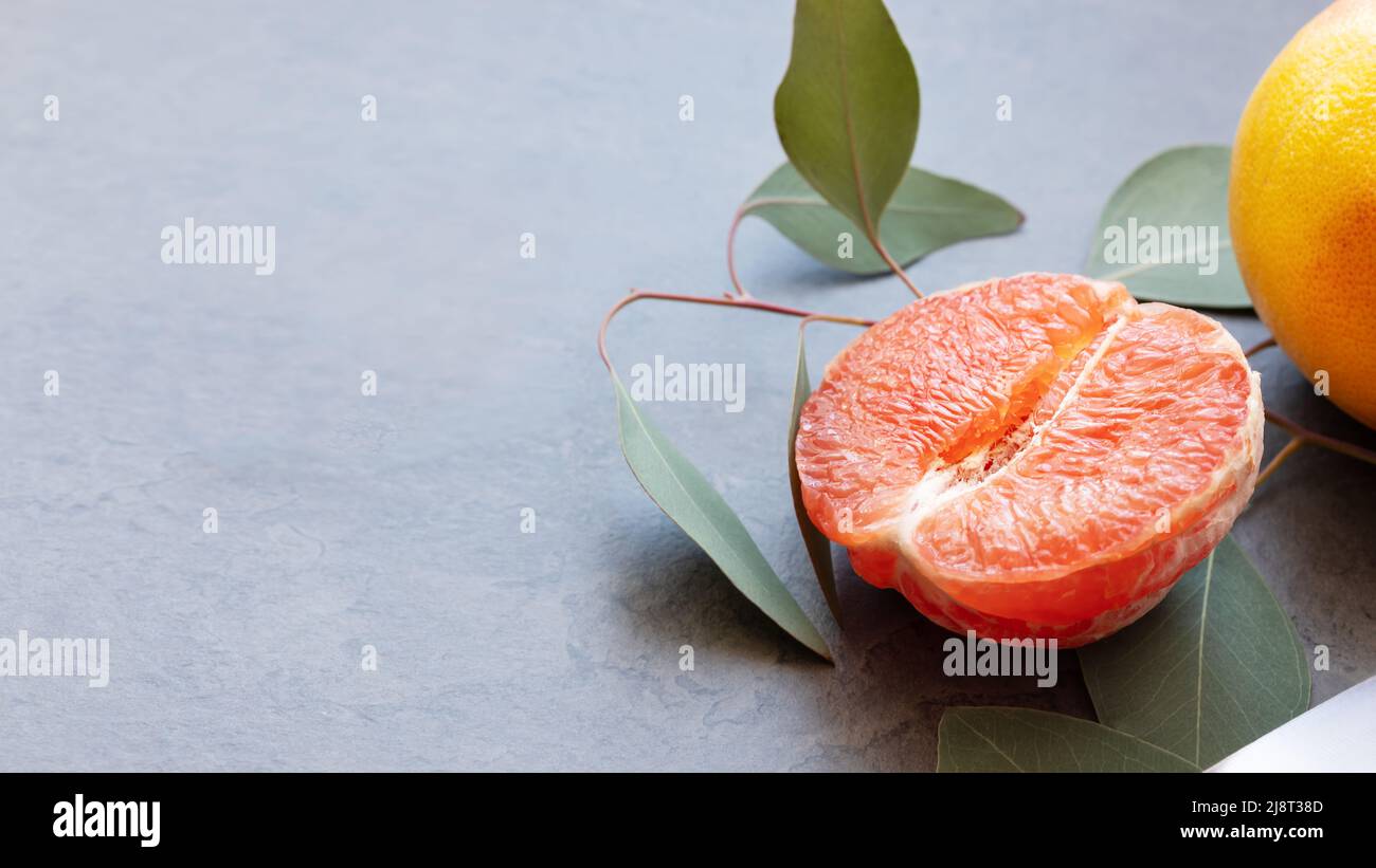 Half a fresh, juicy natural grapefruit with leaves and knife on dark ...