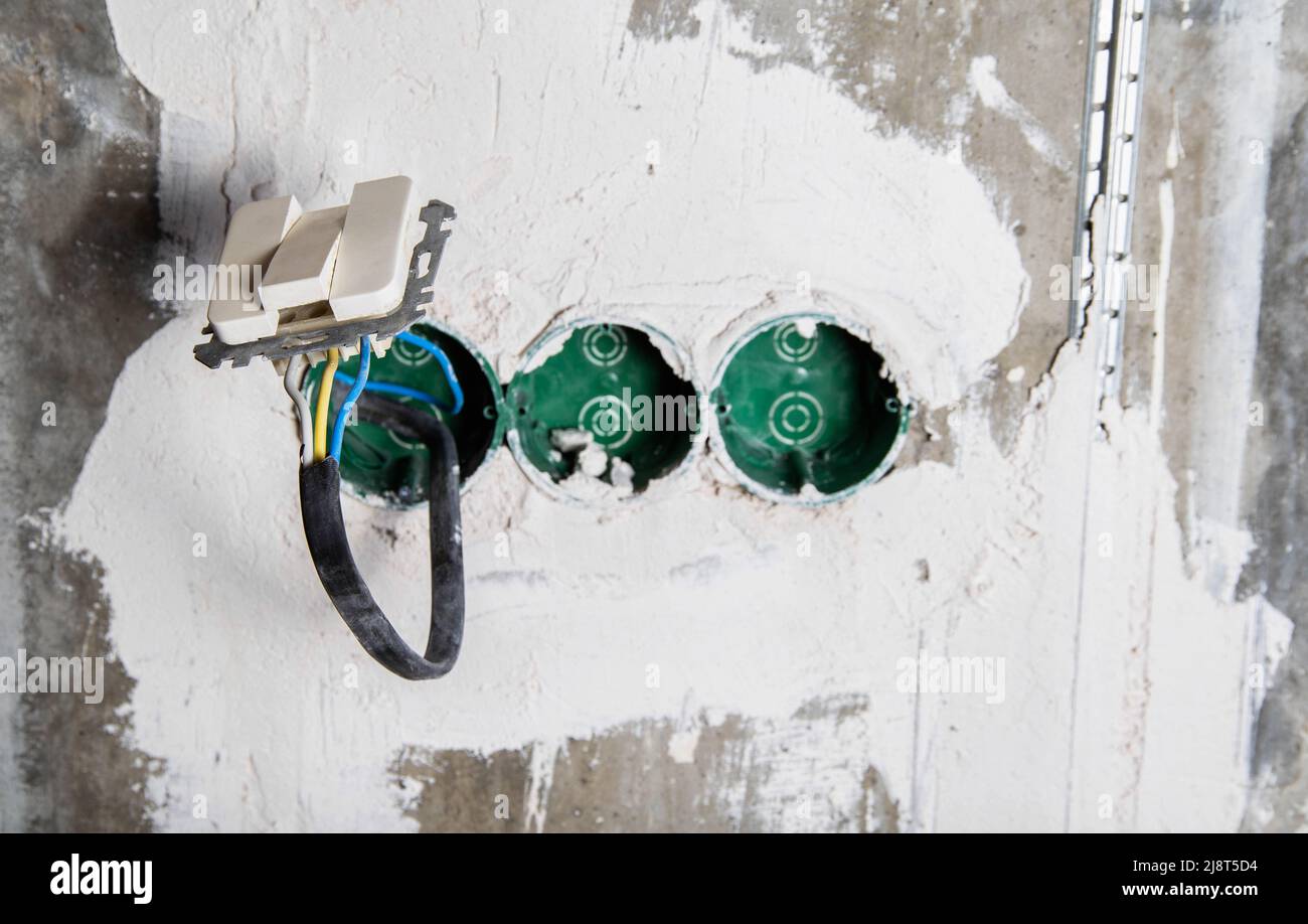An electric switch hangs on wires from socket boxes built into a ...