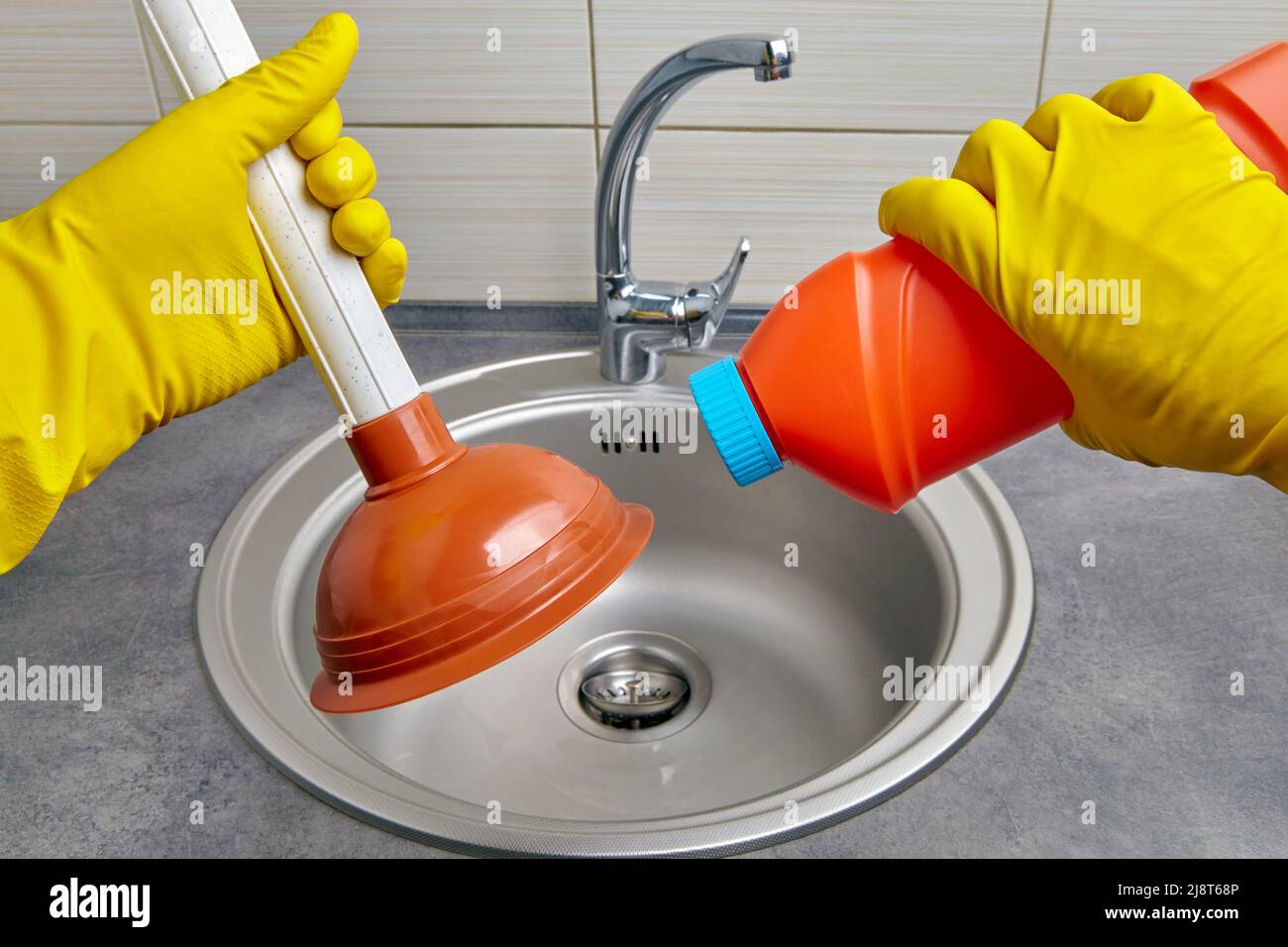 Hands in yellow rubber gloves hold a plunger and a pipe cleaner against ...