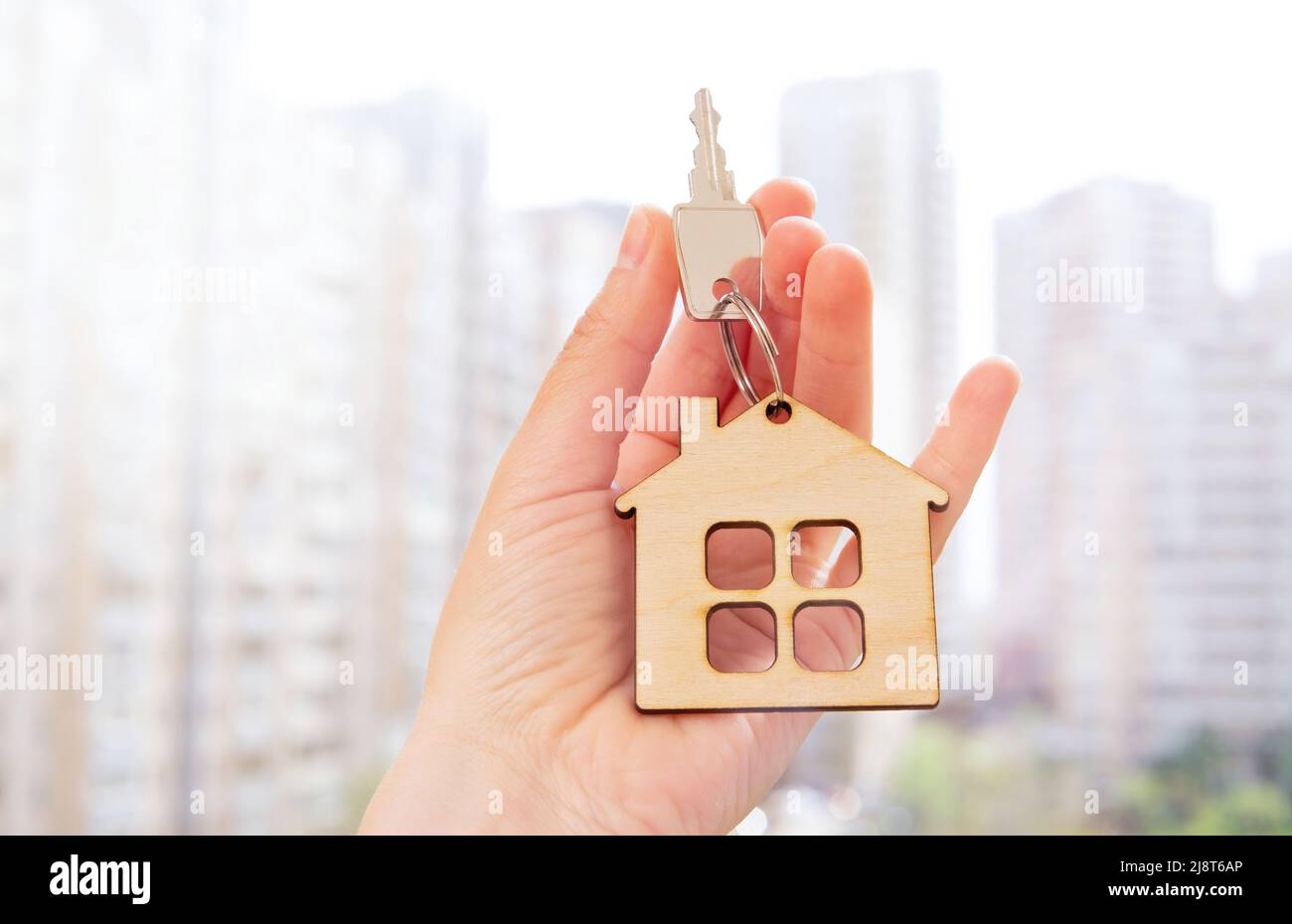 Hand holding a silver toned key with a house shaped keychain against a ...