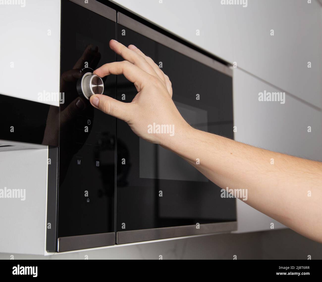 A man's hand twists a regulator button on a modern microwave oven panel ...
