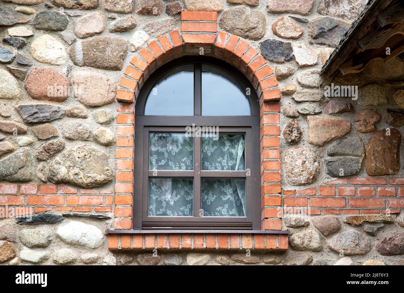 An old wooden semicircular window lined with bricks in a stone building ...