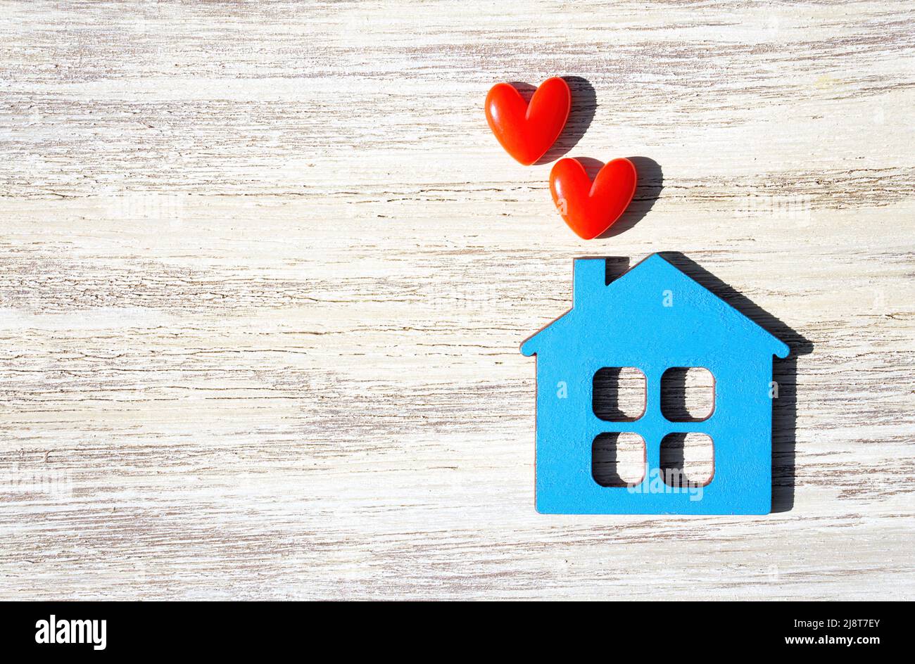 Flat blue house shape with two small red hearts on a wooden table with ...