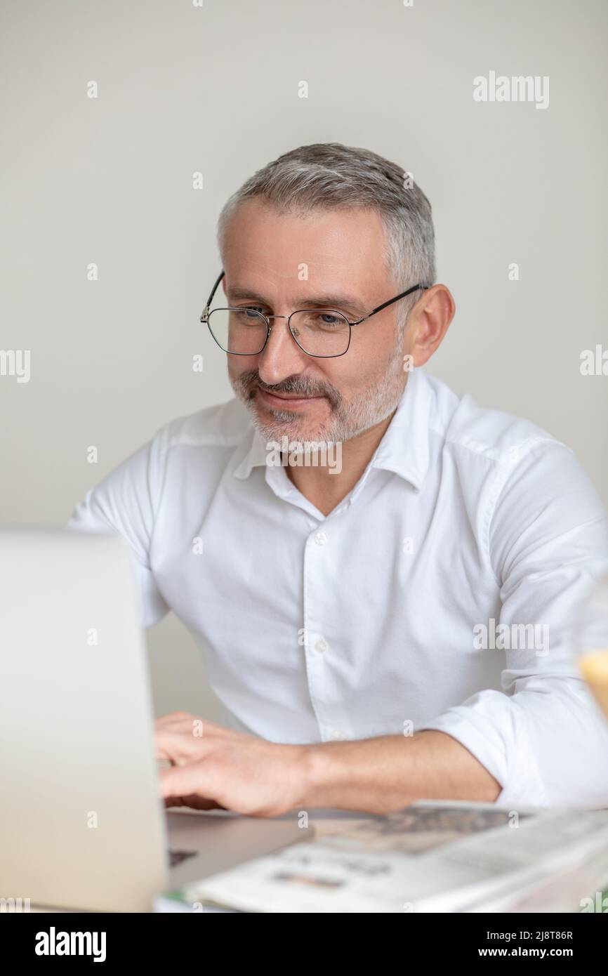 A man in white shirt and eyewear working in the offcie and looking ...