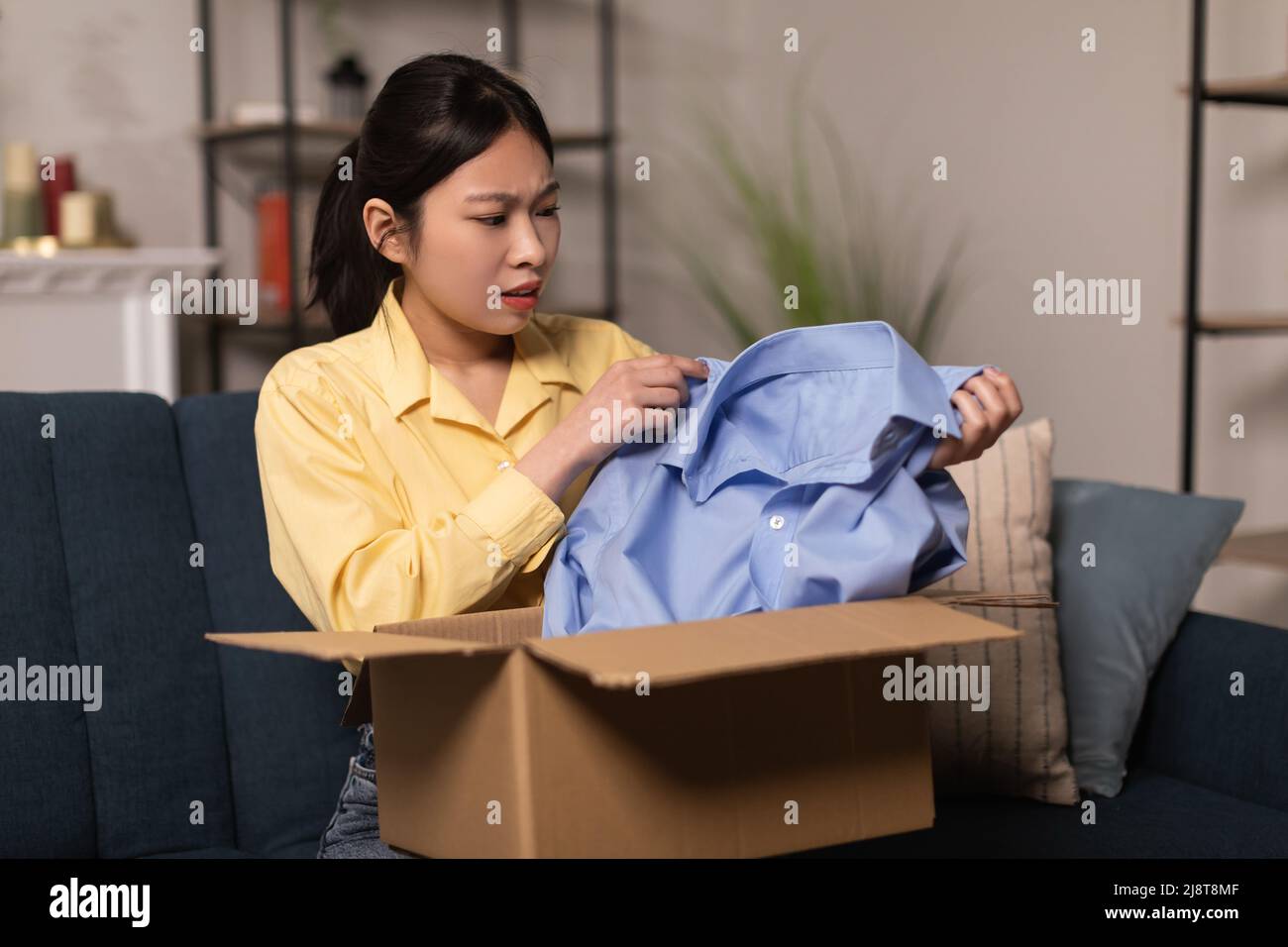 Confused young Asian woman unpacking wrong parcel, delivery mistake ...