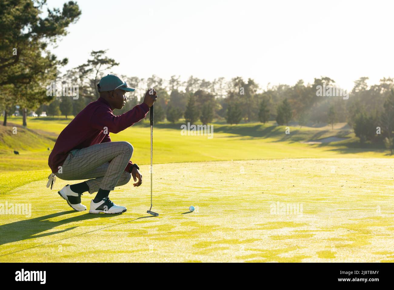 African american young man with golf club and ball crouching against ...