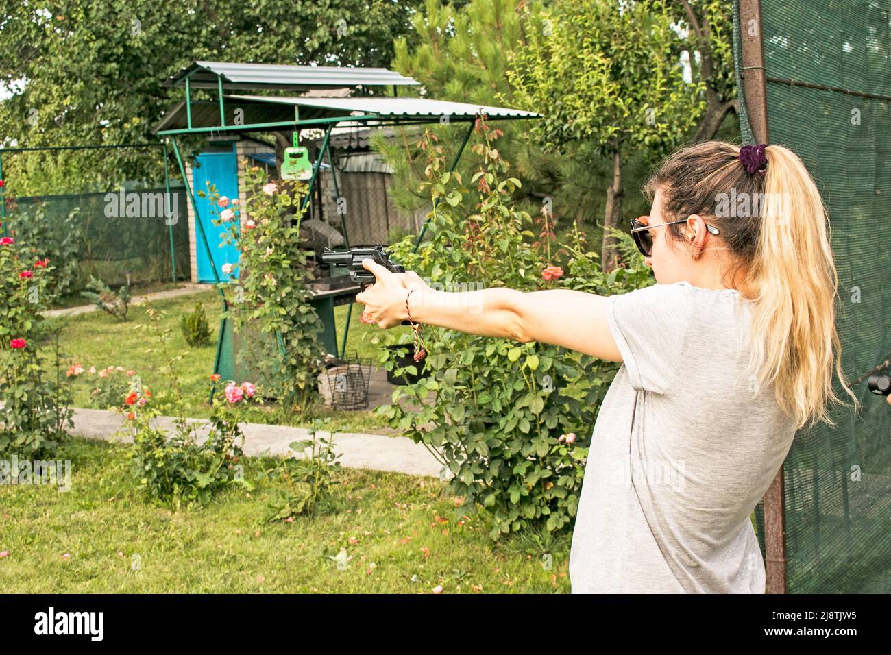Young pretty woman with a gun. The girl in black glasses takes aim at ...