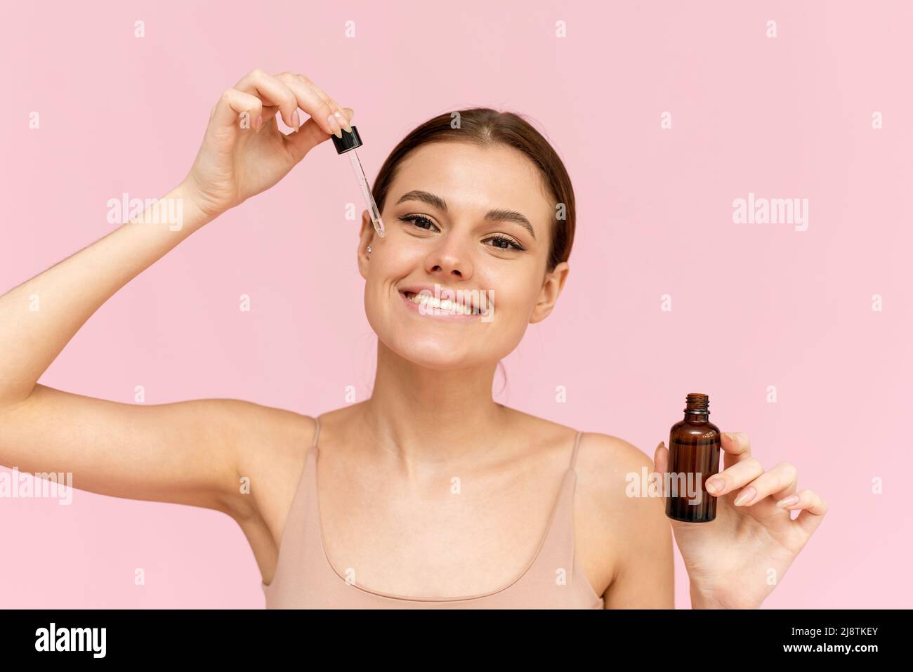Beautiful face portrait of young woman is applying face serum on a ...