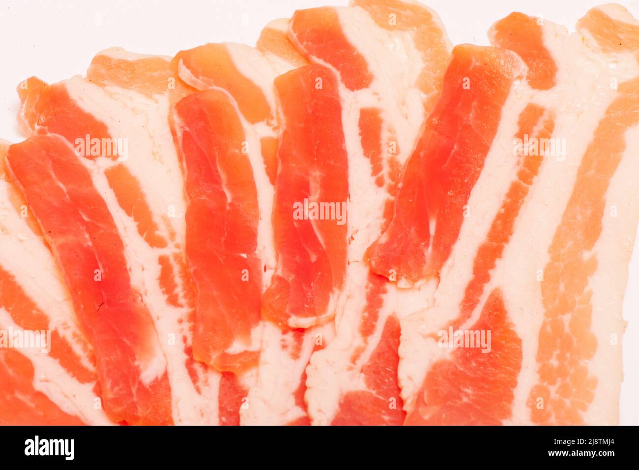Several pieces of bacon cut into strips on a white background Stock ...