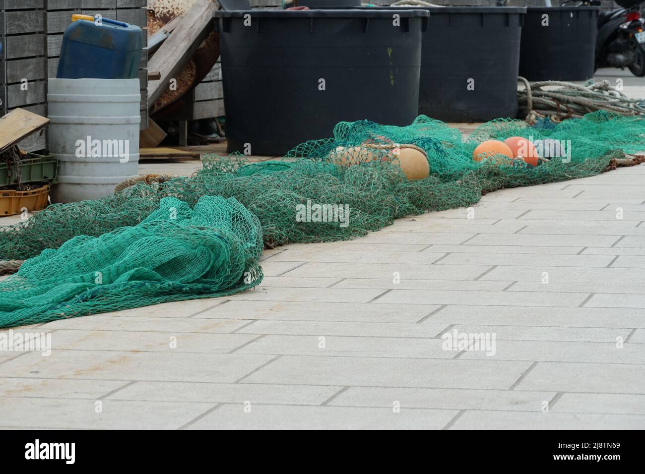 Green fishing net with red-brown floats stretched on the tiled pavement ...
