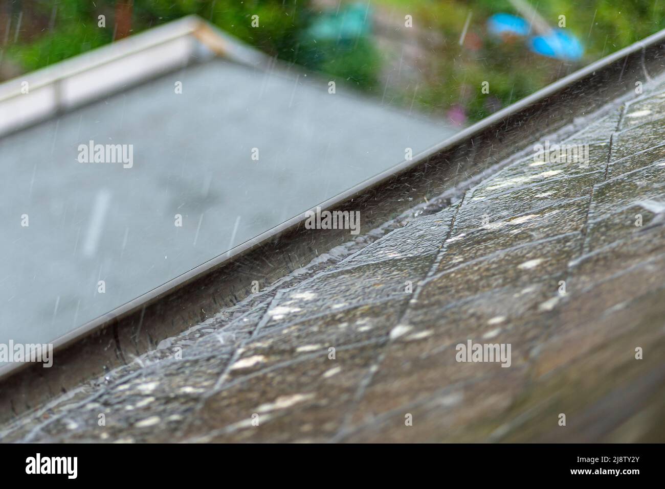 Heavy rain falling on the roof overflowing the gutter with water in ...
