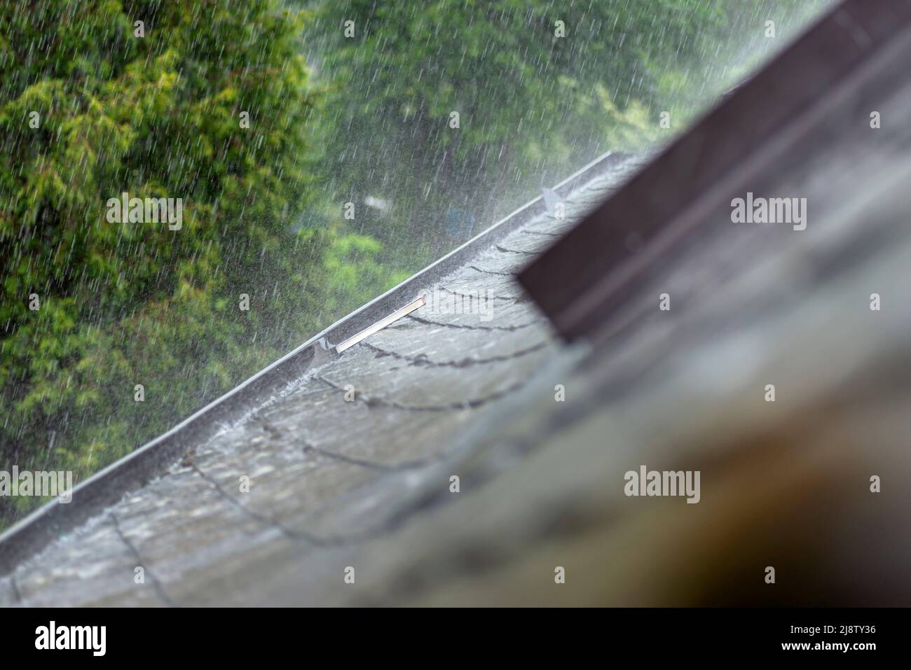 Heavy rain falling on the roof overflowing the gutter with water in ...
