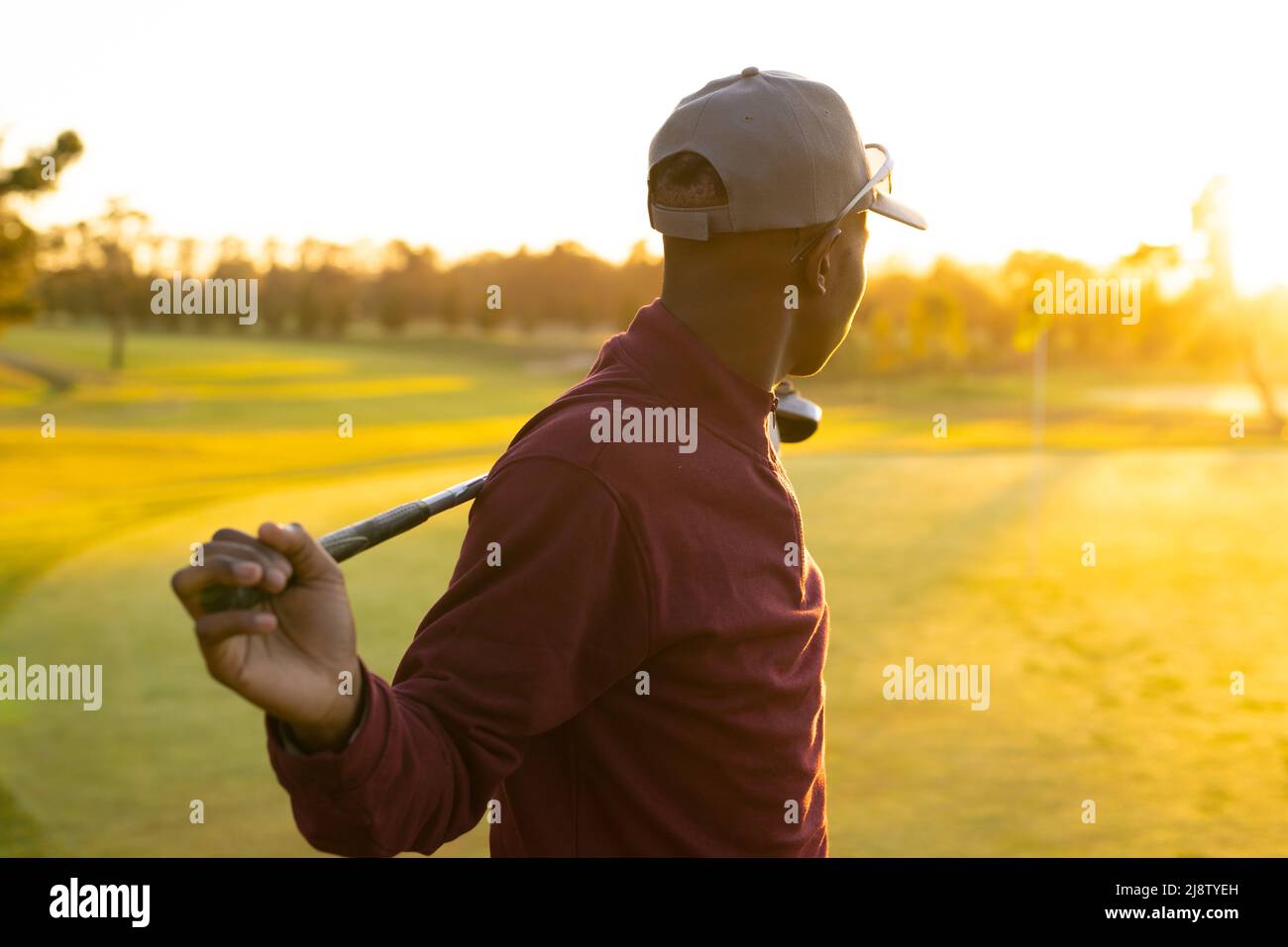 Side view of african american young man wearing cap holding golf club ...