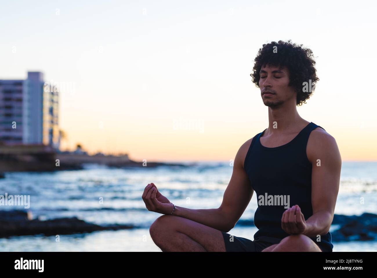 Young african american man with eyes closed meditating at beach during ...