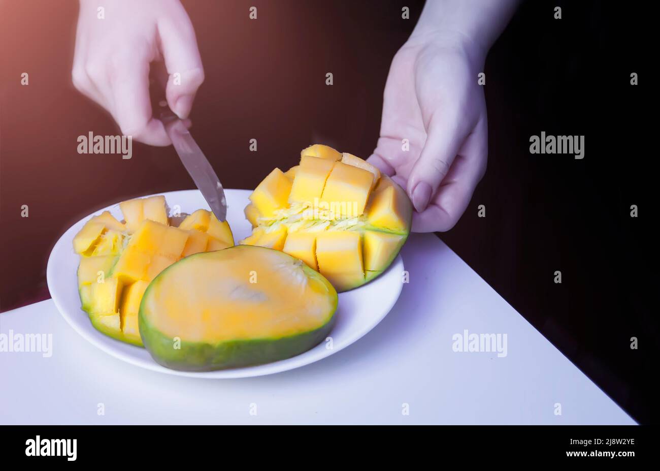Woman cuts the fresh ripe mango into cubes for the fruit pulp easily ...