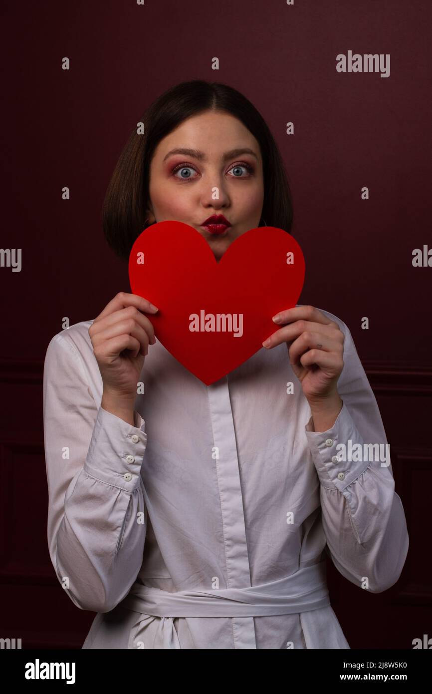Short-haired woman with wide-open eyes and lips shaping kiss on red ...