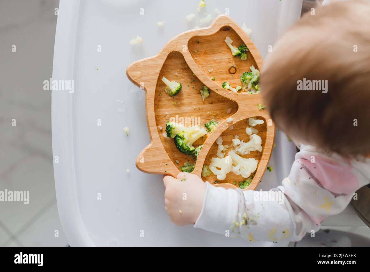Soiled toddler eats boiled vegetables with his hands awkwardly while ...