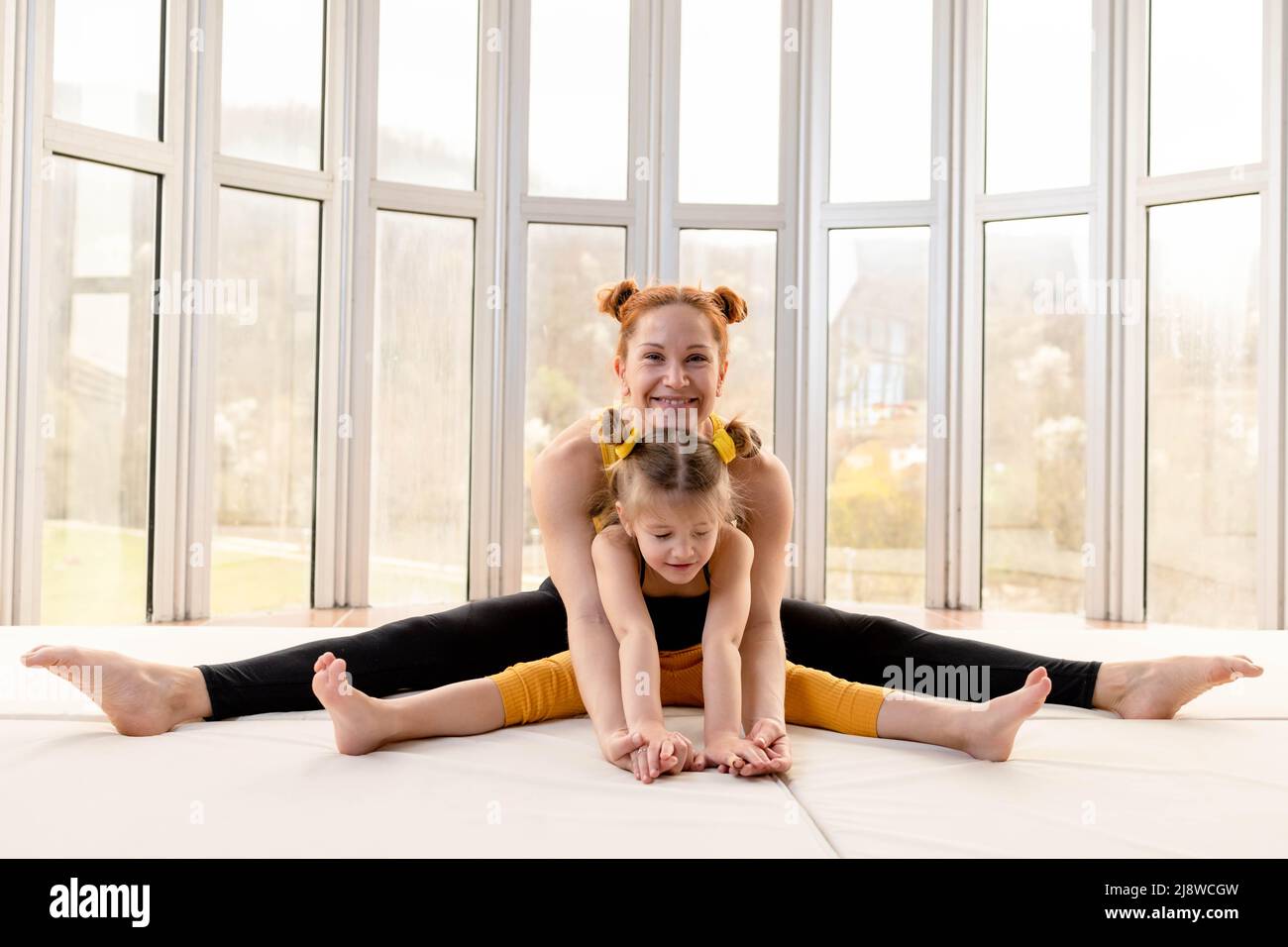Young fit mother and her daughter doing synchronized split Stock Photo ...